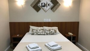 Cama bem arrumada com almofadas florais, duas mesas de cabeceira com abajures e um aplique na parede.