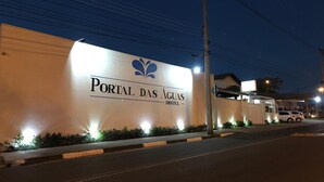 Exterior do Hotel Portal Das Águas com sinalização iluminada, fachada limpa e área de estacionamento visível.