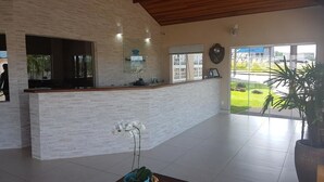 Uma área de recepção com parede de tijolos brancos, teto de madeira e uma grande janela com vista para o exterior.