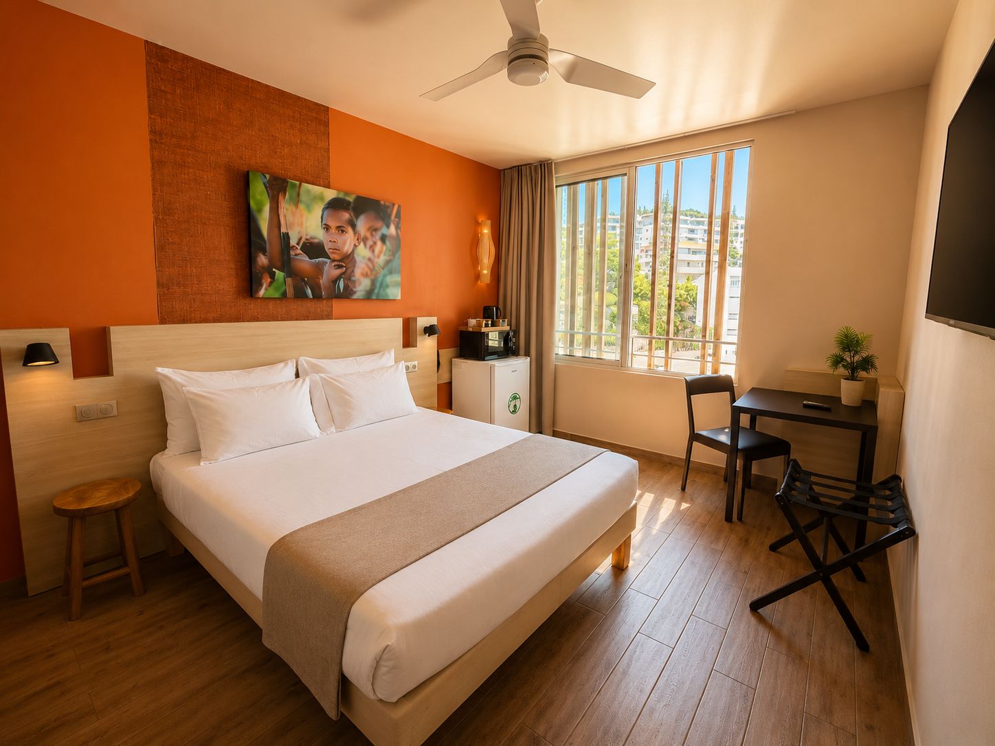 Quarto de hotel com cama, escrivaninha, cadeira, cafeteira e janela com vista.