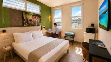 Quarto de hotel com cama, escrivaninha, cadeira e televisão.