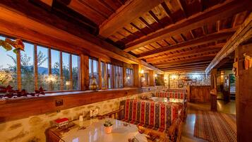 Uma sala de jantar espaçosa com vigas de madeira, grandes janelas e uma mesa posta tradicional.