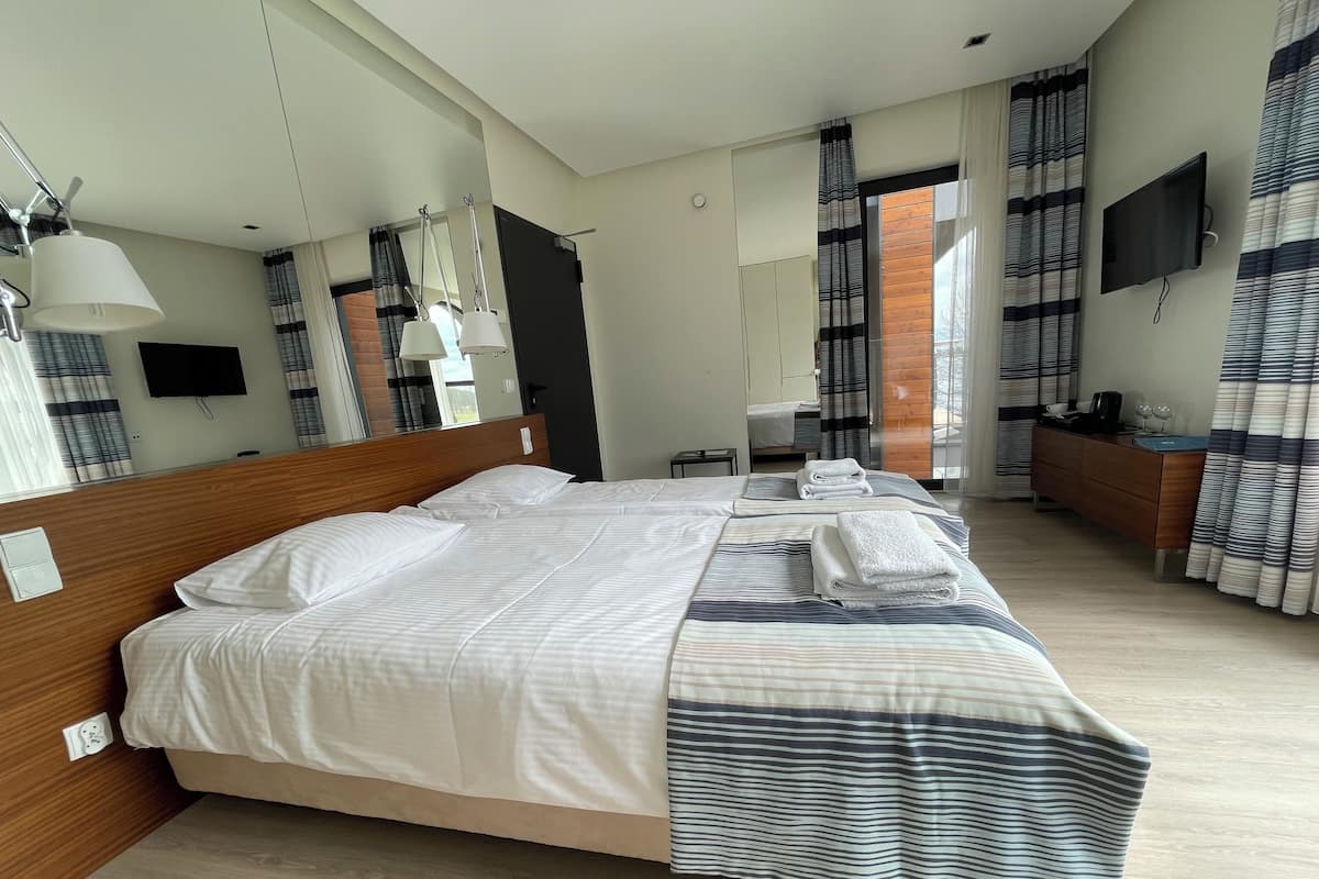 Quarto de hotel moderno com uma cama grande, uma mesa de cabeceira, uma televisão e vista para o exterior.