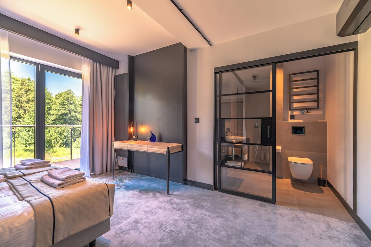 Quarto de hotel moderno com uma cama grande, uma escrivaninha e casa de banho com divisória de vidro.