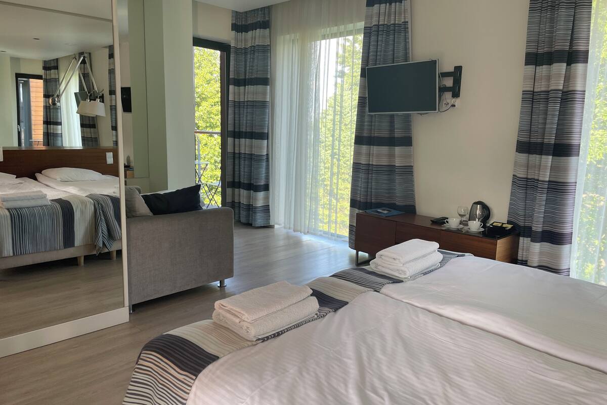 Quarto de hotel moderno com uma cama grande, um sofá, uma escrivaninha com televisão de tela plana e uma varanda com cortinas.
