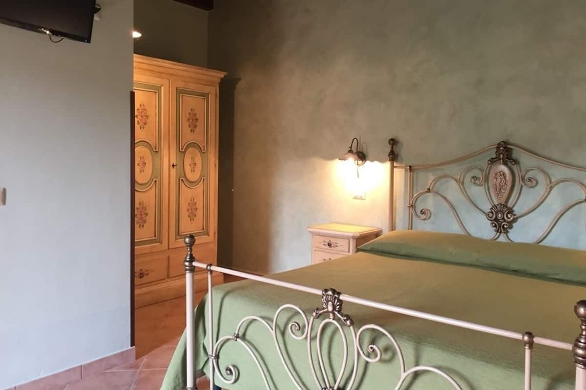 Quarto com cama, mesa de cabeceira, guarda-roupa e televisão na parede.