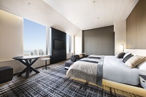 Quarto de hotel moderno com uma cama grande, uma mesa pequena, um sofá e uma televisão.