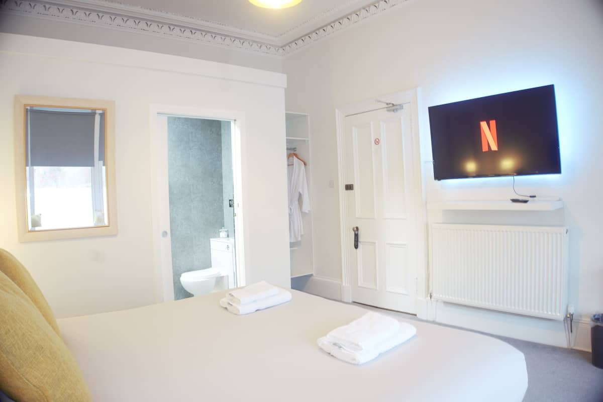 Quarto de hotel com cama, televisão na parede, porta e janela.