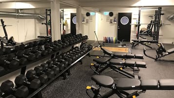 Uma academia com fileiras de halteres, bancos e equipamentos de exercícios.