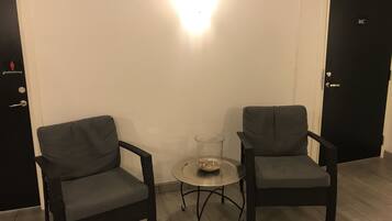 Duas cadeiras e uma pequena mesa em um quarto com um luminária na parede e uma porta com a inscrição 'WC'.