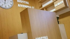 Um balcão de recepção de madeira com a inscrição "HOSTAL AVENTURA 57" e um relógio na parede.