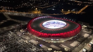 Um estádio grande com design circular, rodeado por estacionamentos e alguns edifícios menores.
