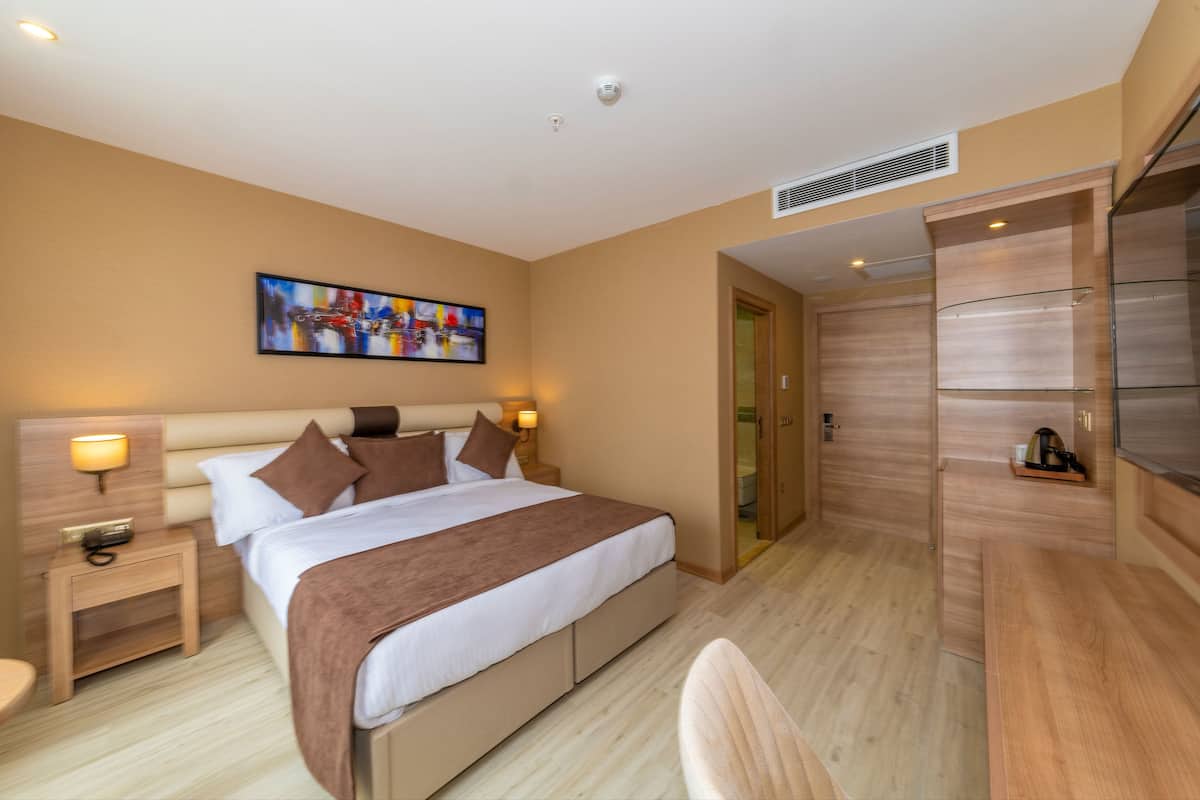 Quarto de hotel com uma cama grande, mesas de cabeceira, um quadro na parede e um guarda-roupa de madeira.