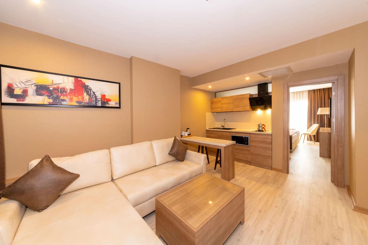 Quarto de hotel moderno com sofá, mesa de centro de madeira, área de cozinha e mesa de jantar.