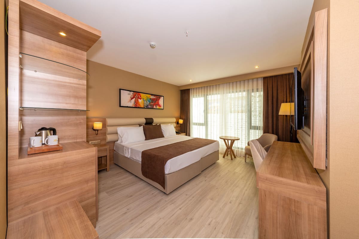 Quarto de hotel moderno com uma cama grande, uma escrivaninha, uma televisão e uma janela com cortinas.