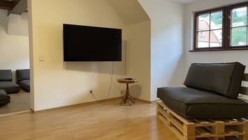 Uma sala de estar moderna com uma televisão de tela plana na parede, um sofá de palete de madeira e uma pequena mesa lateral de madeira.