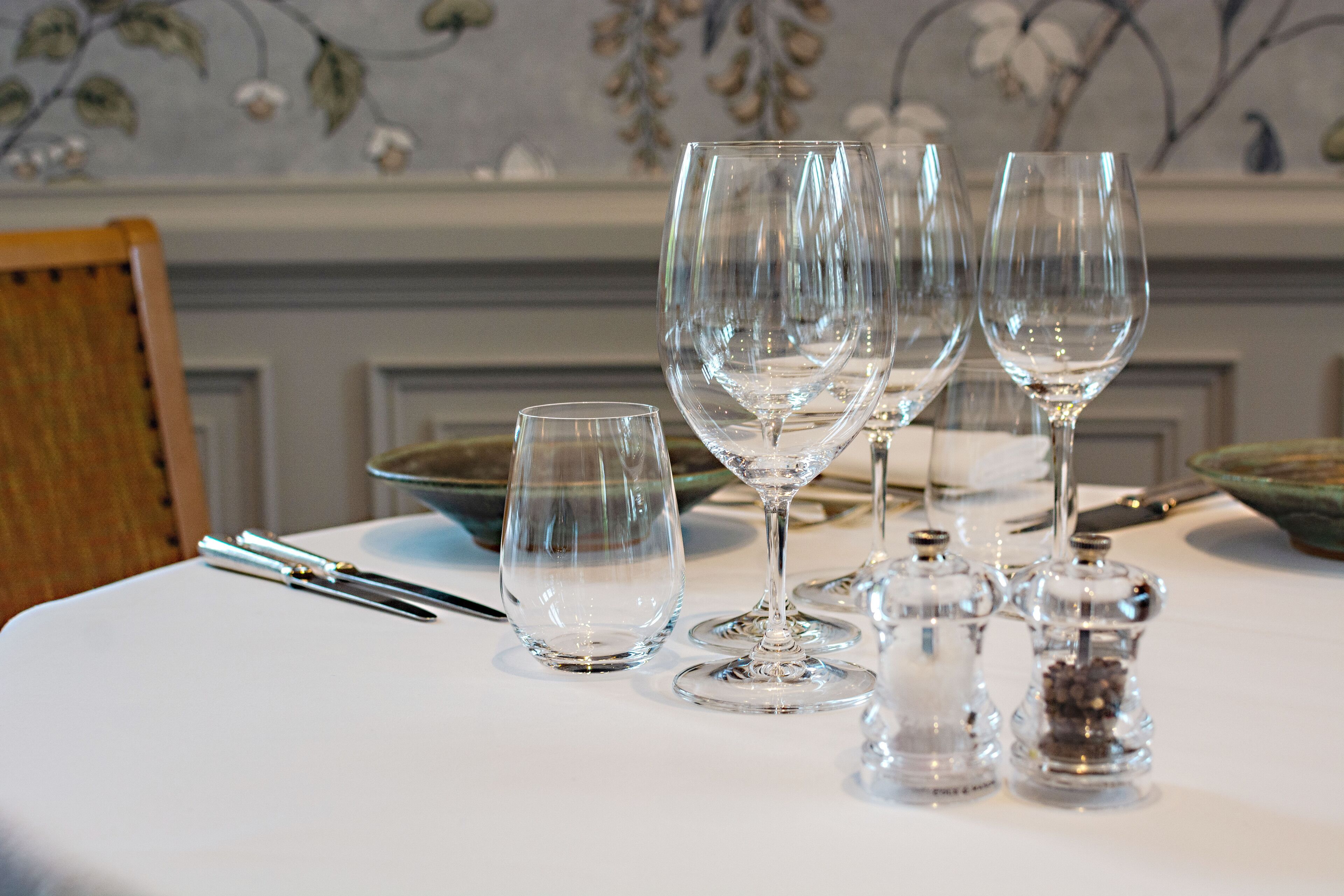 Uma mesa posta com taças de vinho, saleiro e pimenteiro, e uma faca.
