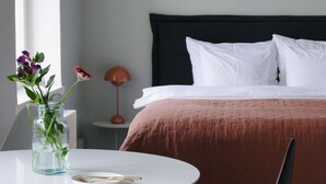 Quarto de hotel com cama, mesa redonda com um vaso de flores, cadeira e abajur.