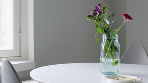 Uma mesa branca com um pote de vidro com flores, um prato branco e um garfo.