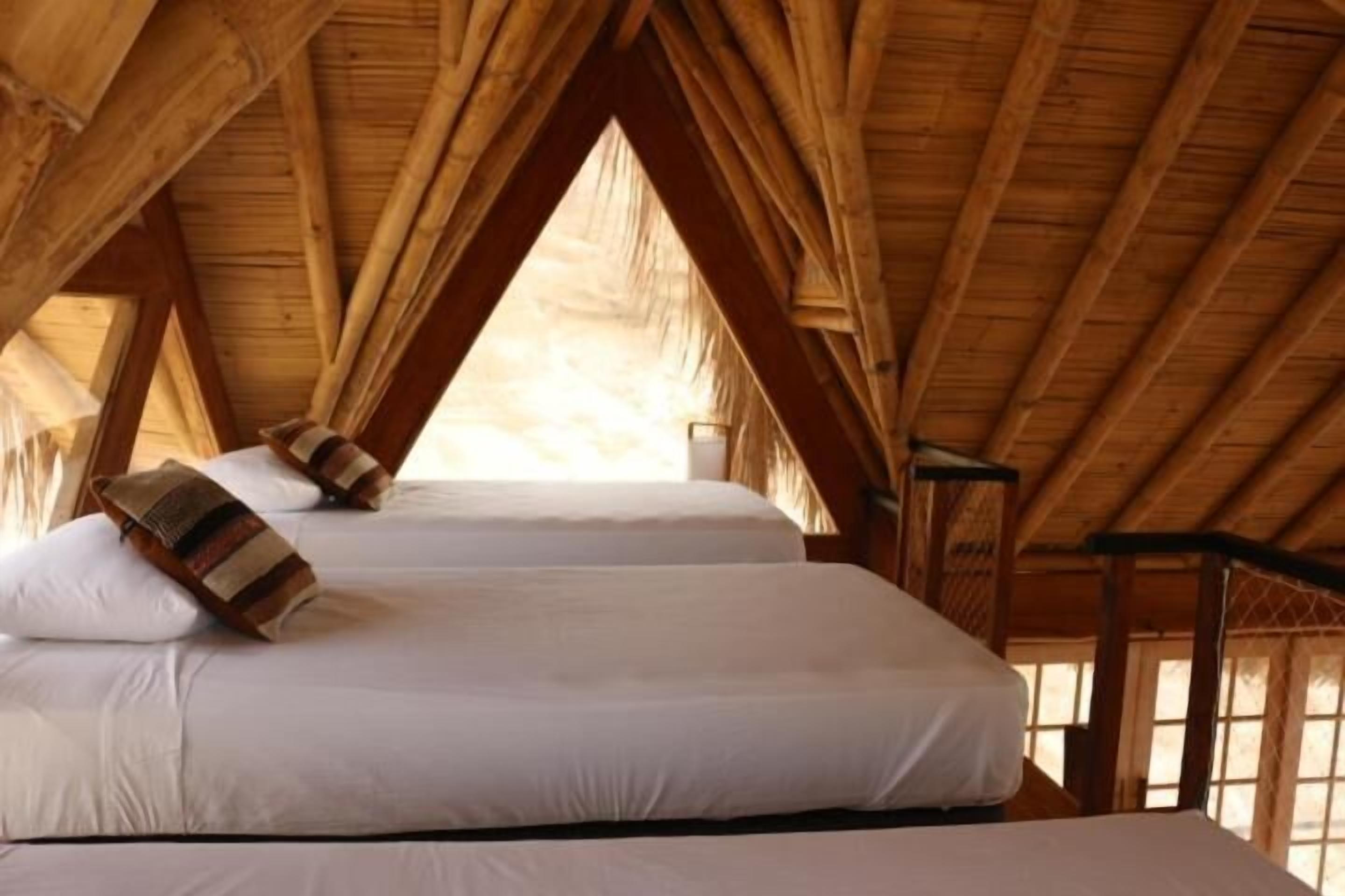 Quarto com duas camas, vigas de madeira e vista pela janela.