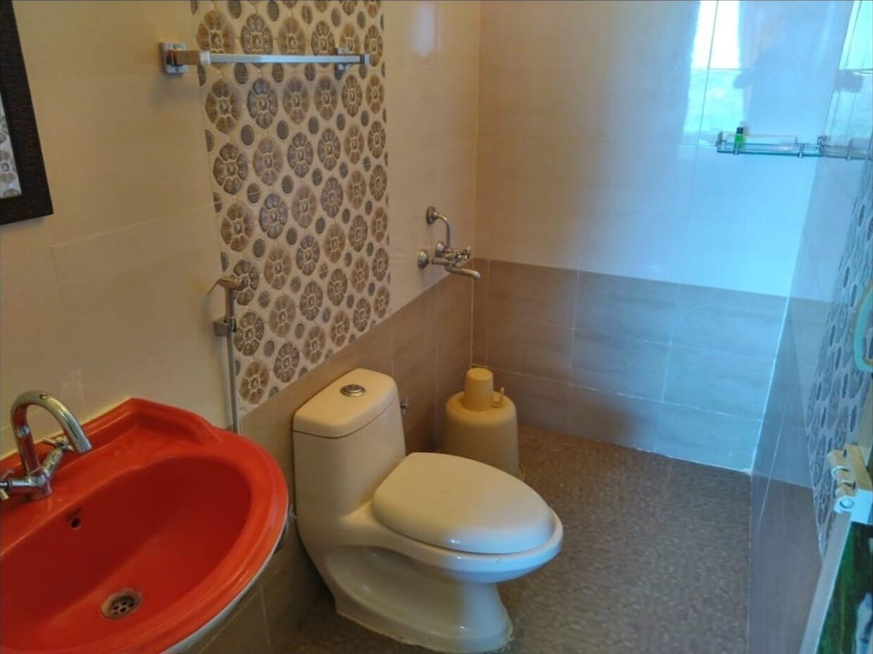 Casa de banho com lavatório vermelho, sanita e zona de duche.