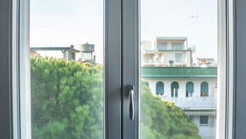 Quarto com duas janelas com vista para um edifício e vegetação.