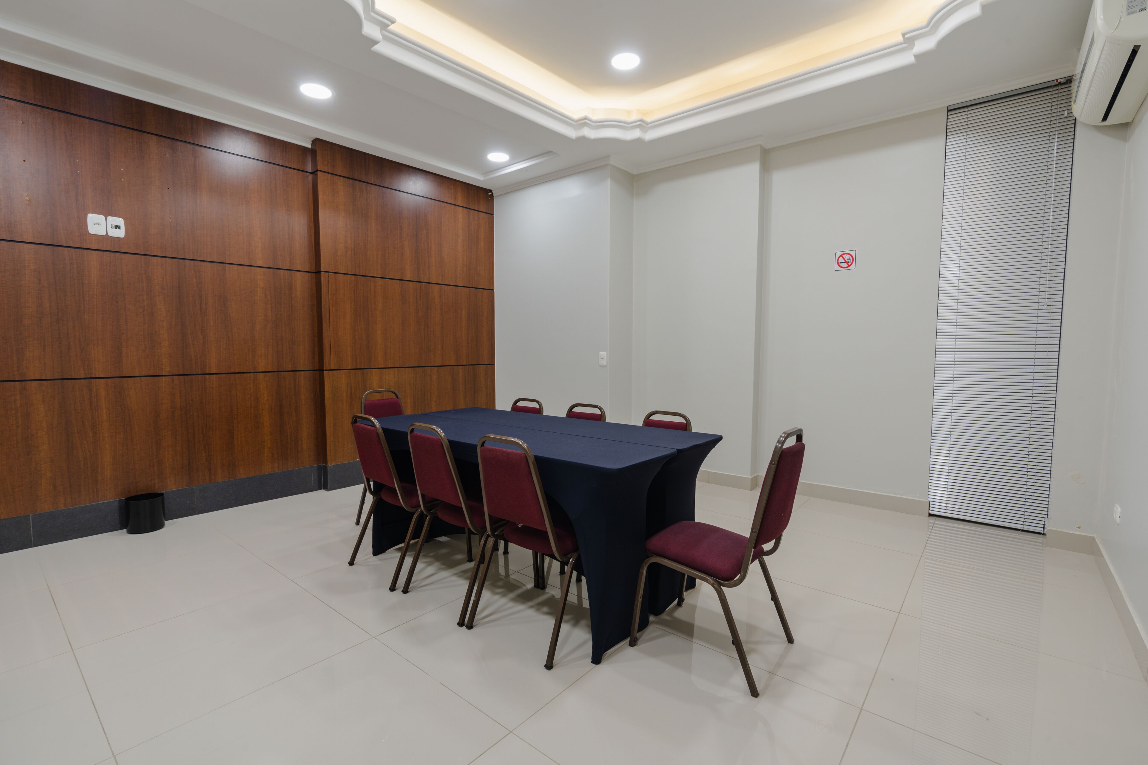 Uma sala de conferências com uma mesa comprida e seis cadeiras, paredes brancas e um painel de madeira em uma das paredes.