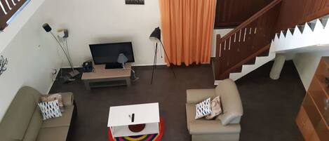 Uma sala de estar ampla com sofás, uma televisão de tela plana, uma mesa de centro e uma escada.