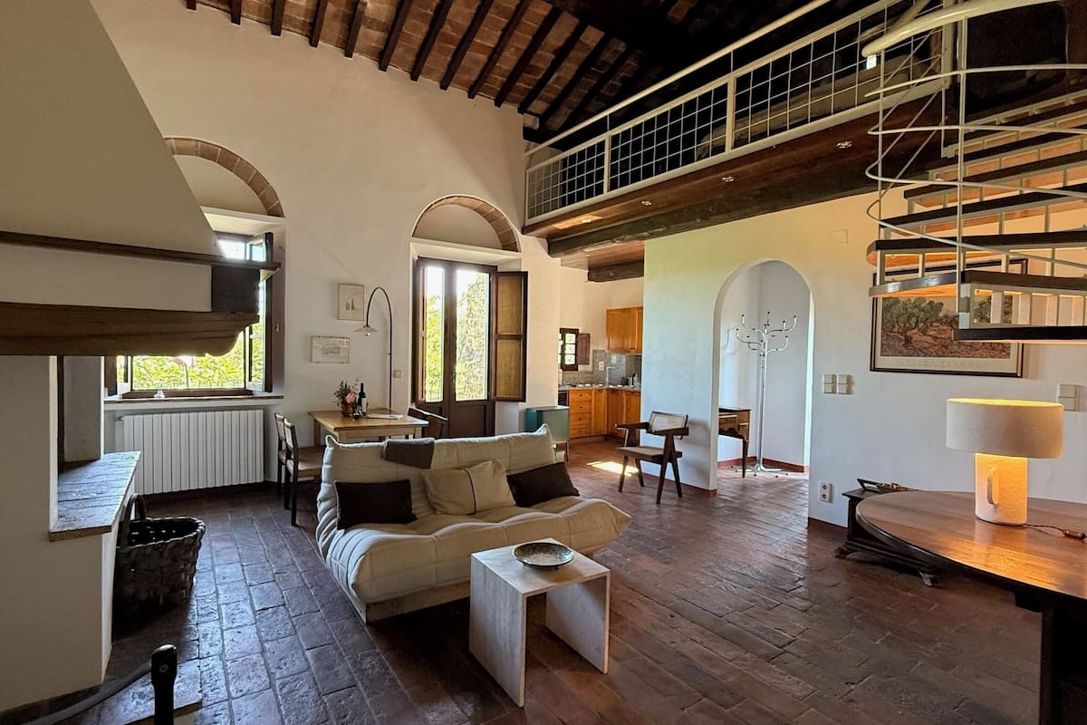 Uma sala de estar ampla, com teto alto, vigas de madeira, cozinha planejada e um aconchegante espaço de estar com lareira.