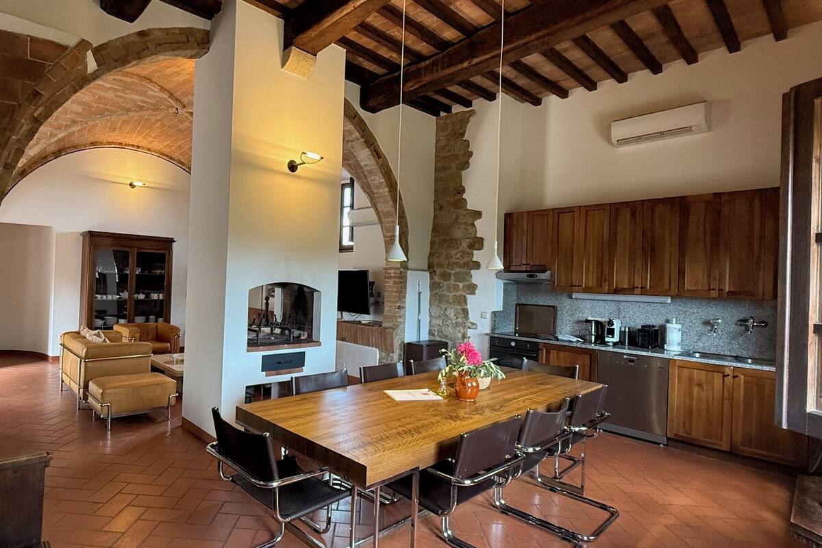 Uma cozinha ampla com armários de madeira, uma mesa de jantar com cadeiras e um arco de pedra.