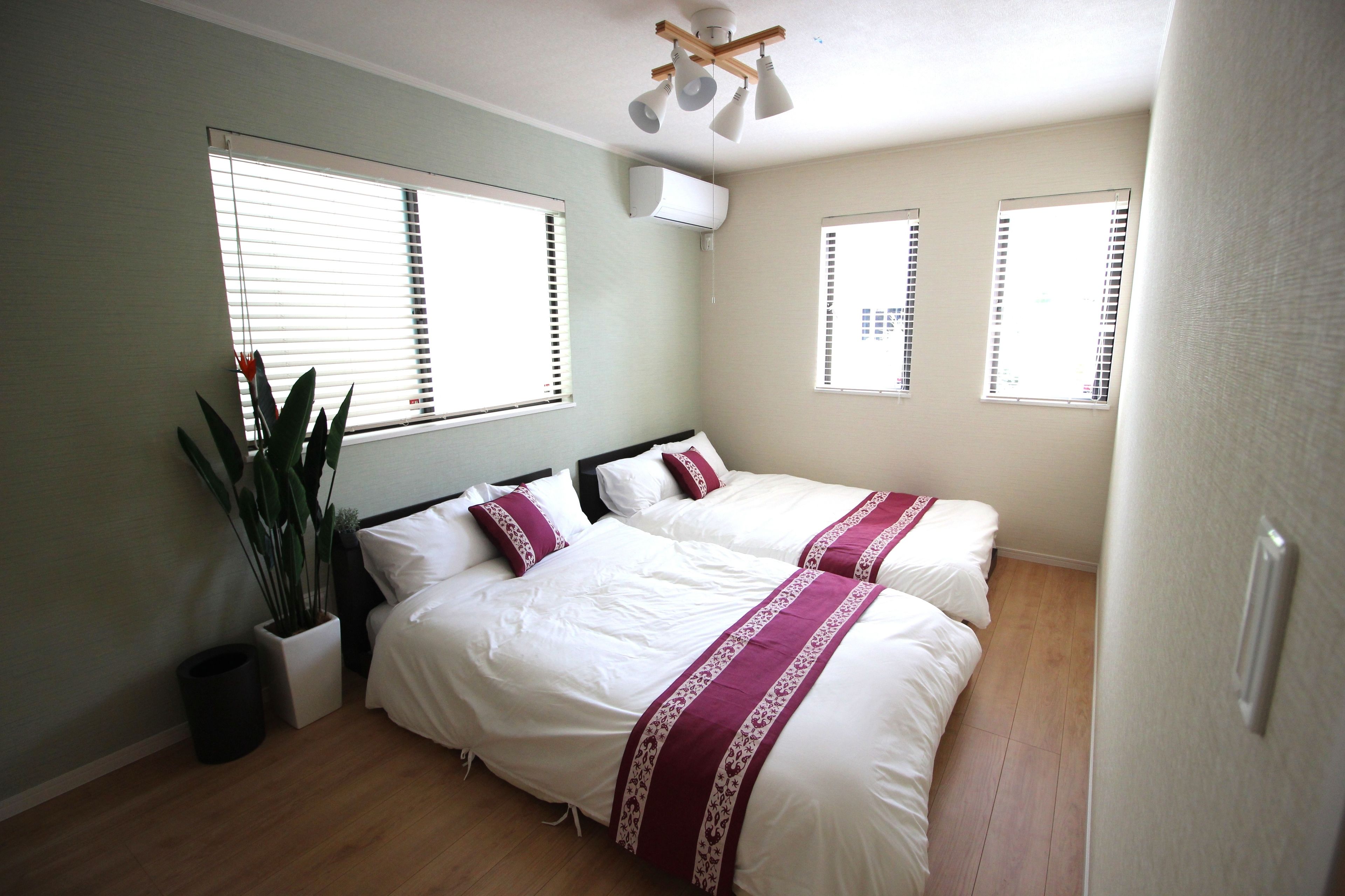 Quarto de hotel com duas camas, uma planta em vaso e um ventilador de teto.