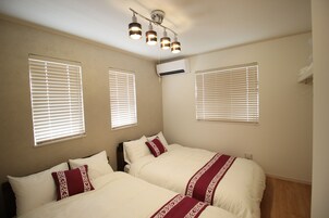 Quarto com duas camas, roupa de cama branca e luminária no teto.