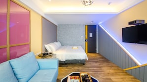 Quarto de hotel moderno com uma cama, um sofá azul, uma televisão e uma luminária esférica única.
