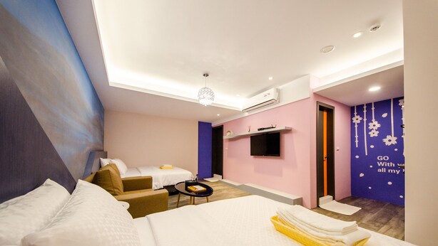 Quarto de hotel moderno com uma cama grande, uma cama menor, uma escrivaninha e uma televisão presa na parede.