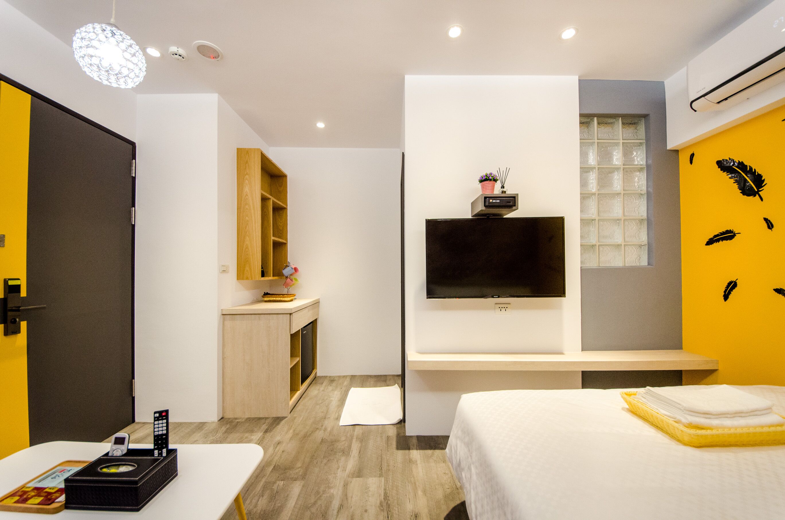 Quarto de hotel moderno com uma cama, uma televisão fixada na parede, uma pequena escrivaninha com uma luminária e uma janela com vista.
