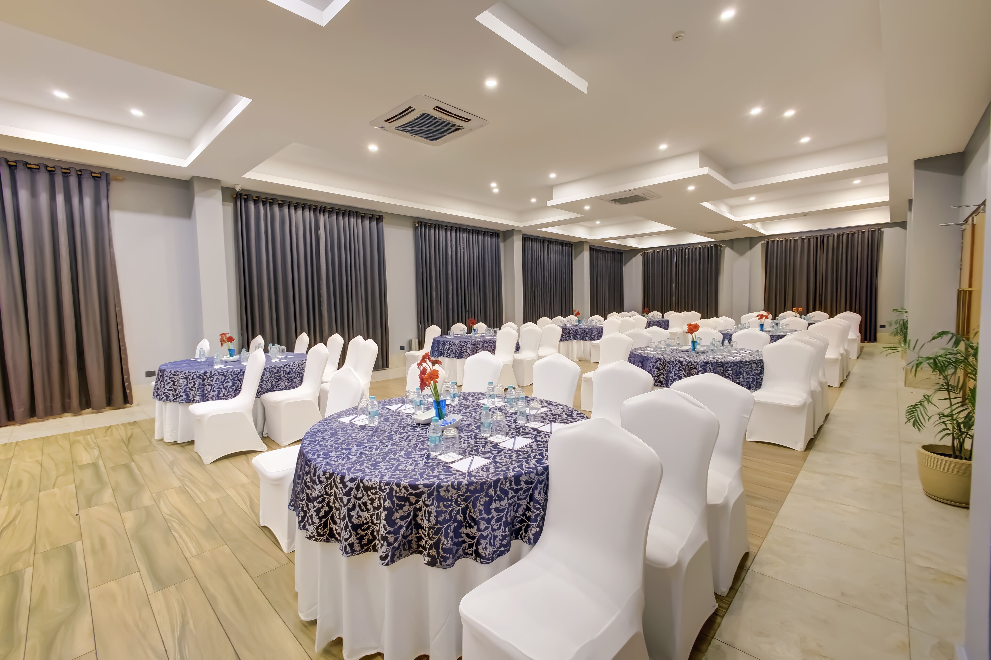 Uma sala de conferências com mesas redondas, cadeiras brancas e toalhas de mesa azuis.