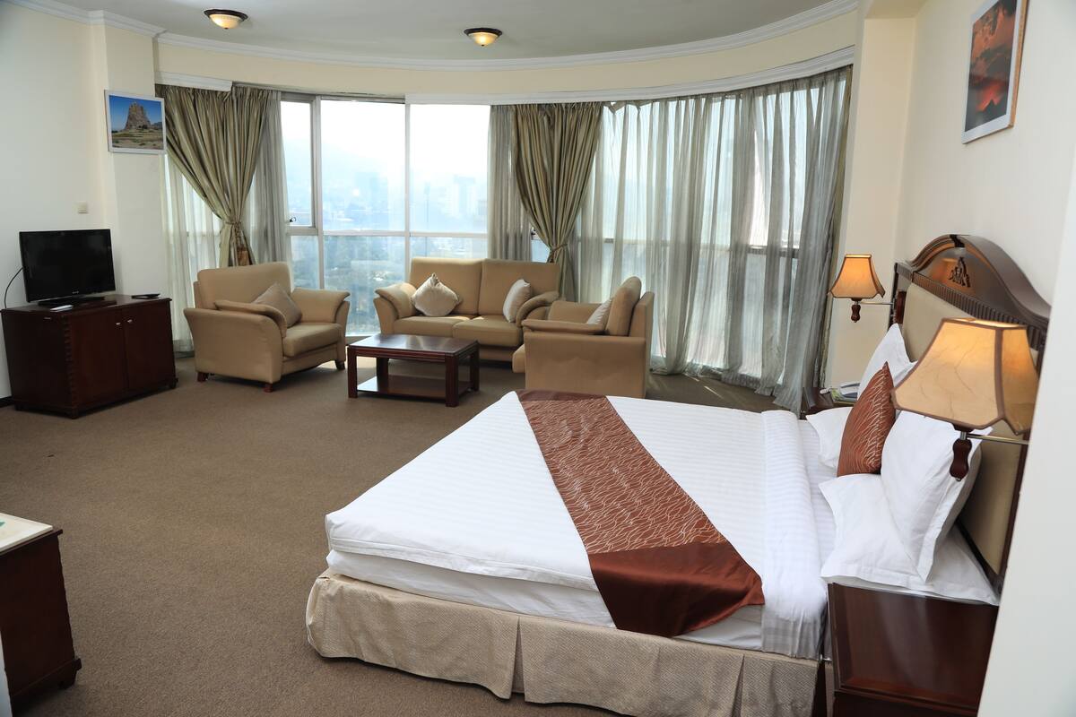 Quarto de hotel com uma cama grande, duas poltronas, um sofá, uma televisão e uma secretária.