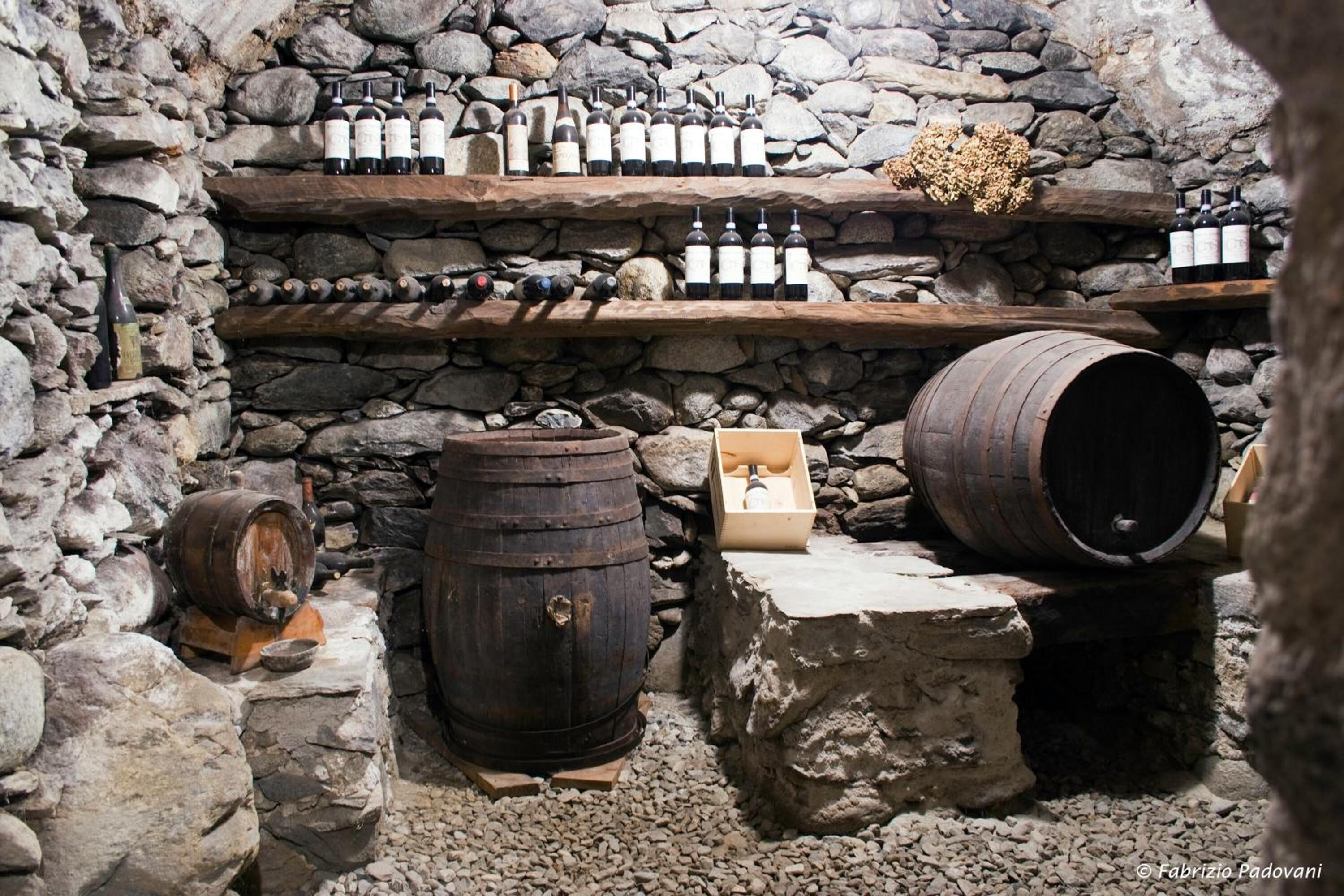 Uma parede de pedra com garrafas de vinho e barris de madeira.
