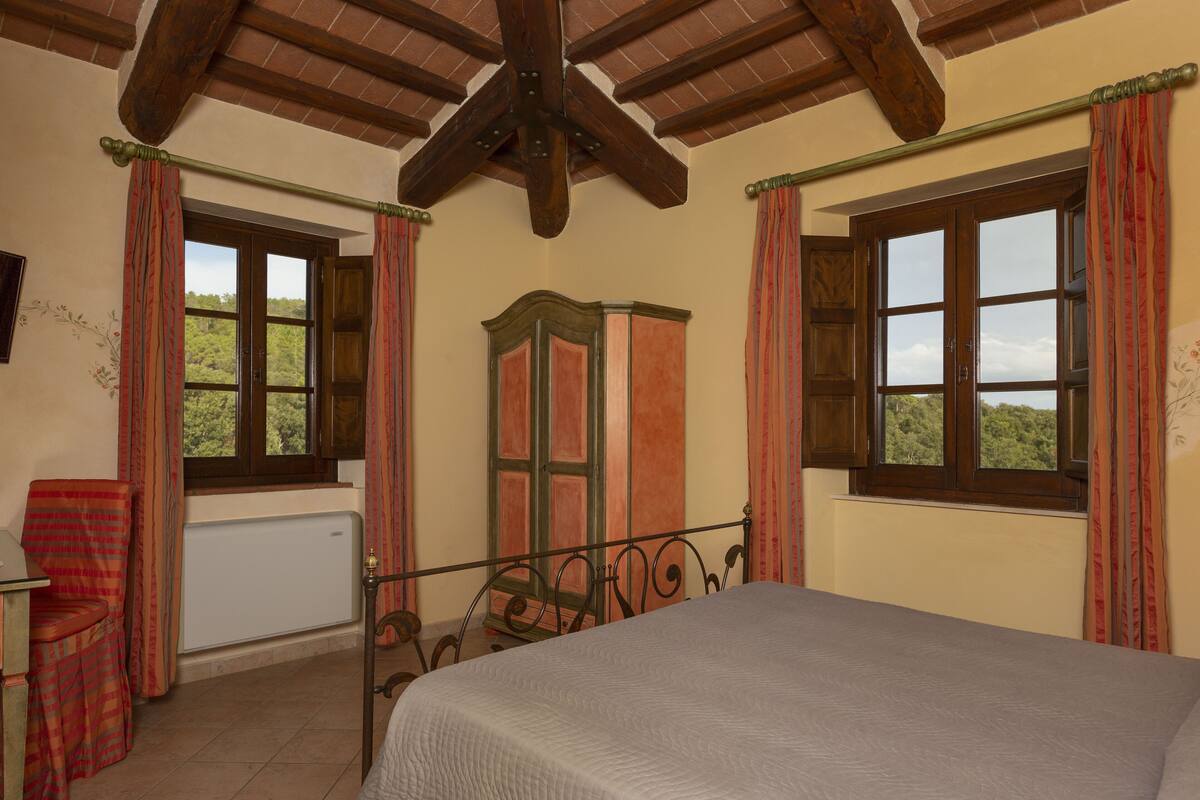 Quarto com cama, duas janelas com cortinas, radiador e guarda-roupa.