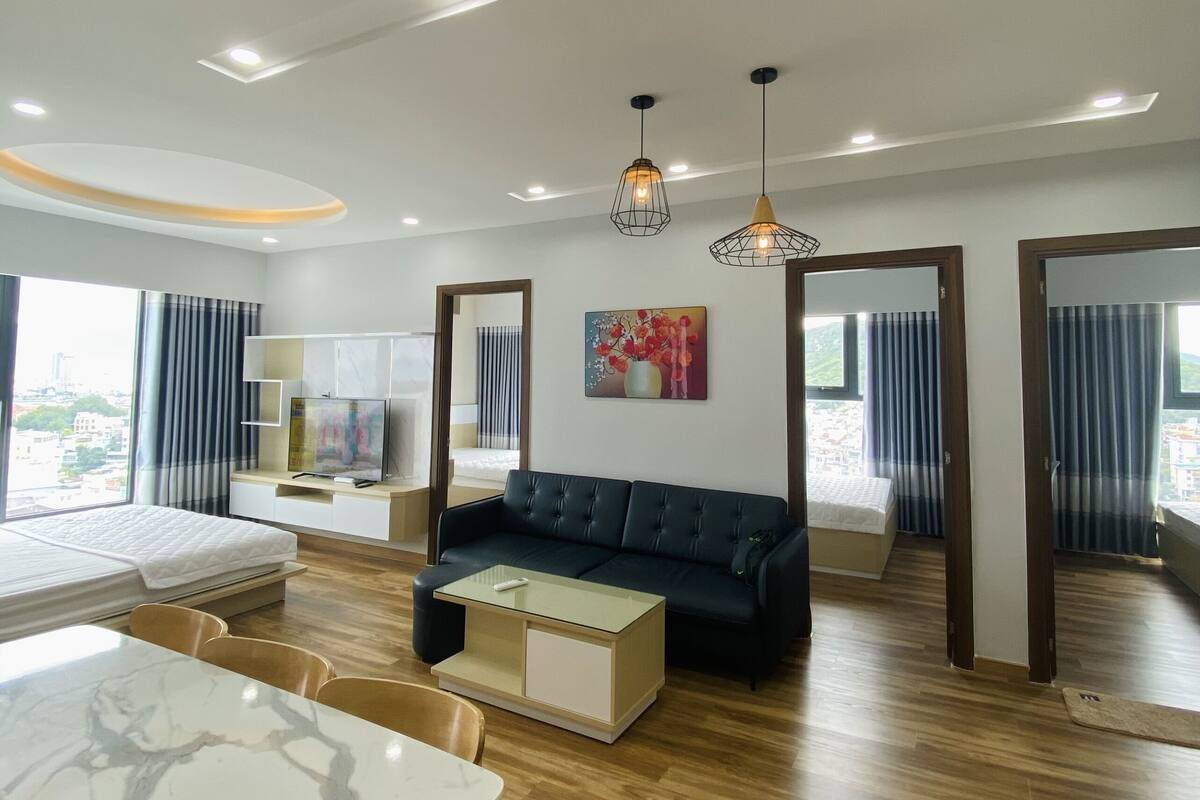 Quarto de hotel moderno com cama, sofá, mesa de jantar e uma grande janela com vista para a cidade.