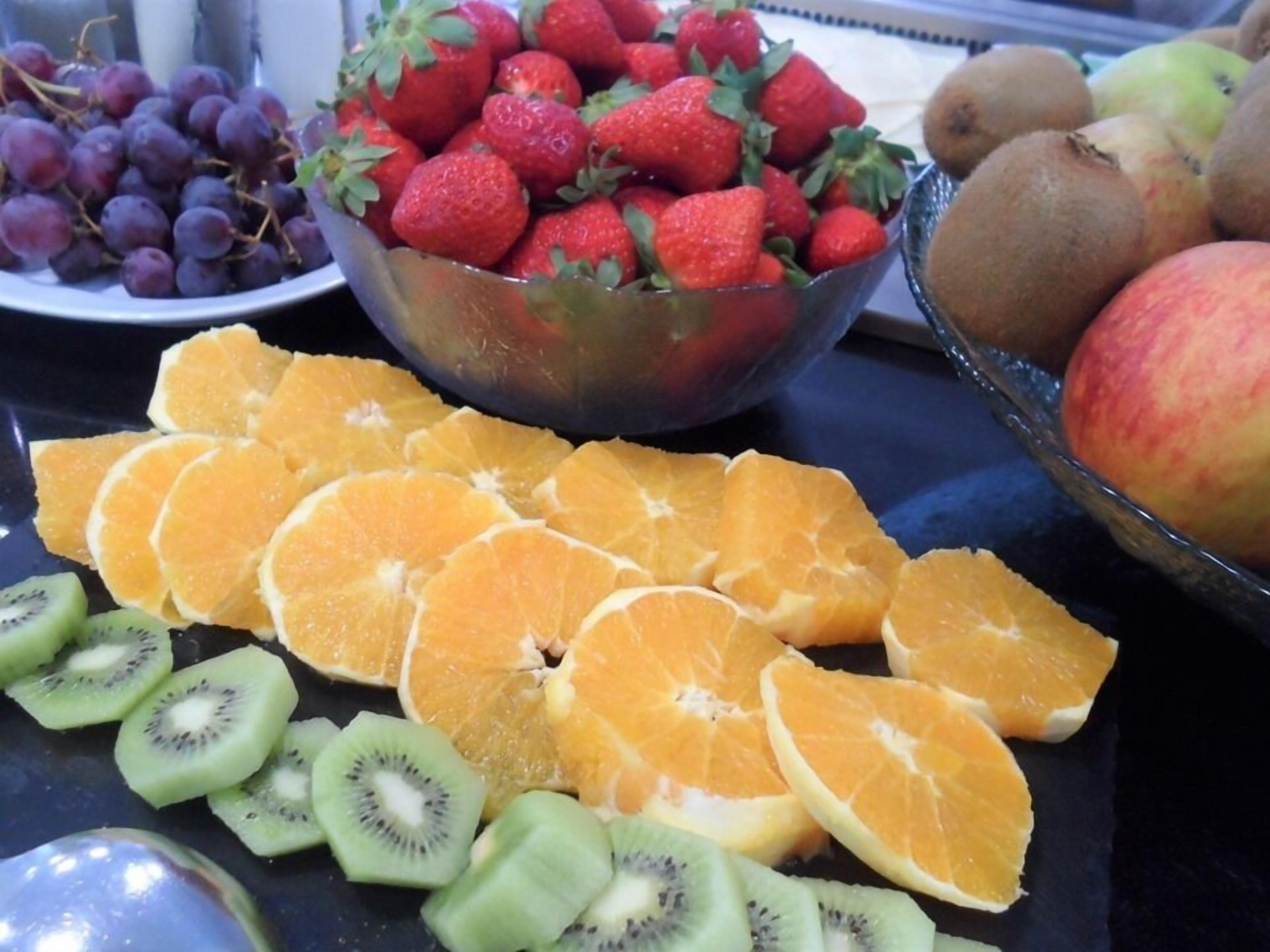 Uma mesa com uma variedade de frutas, incluindo uvas, morangos, kiwis, laranjas e maçãs.