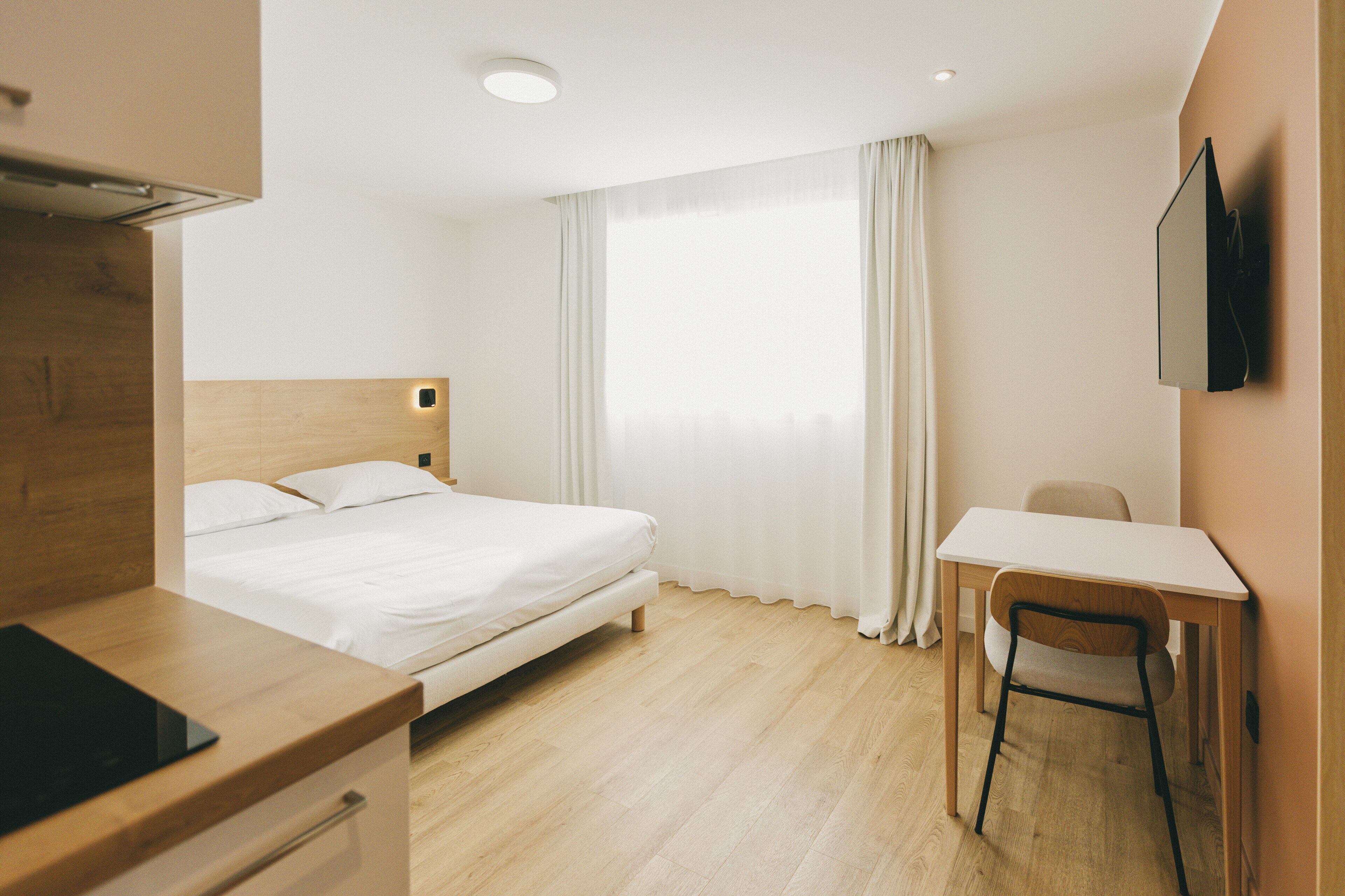 Quarto de hotel com cama, escrivaninha e cadeira.