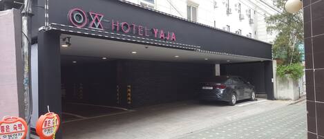 Entrada de hotel com fachada preta e um carro estacionado.