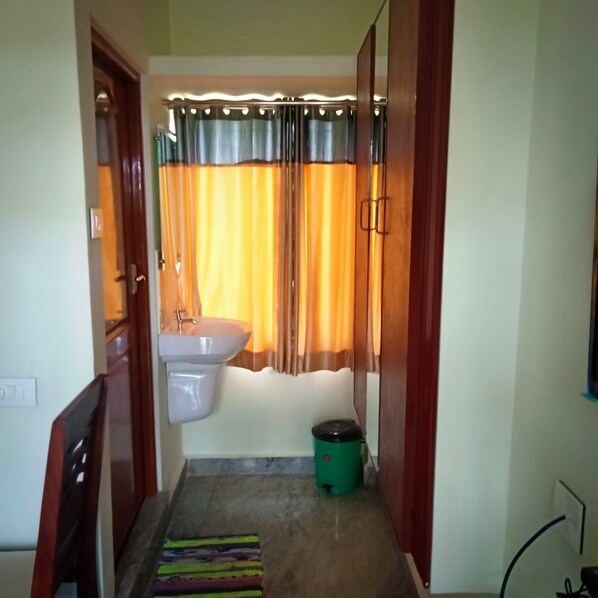 Um corredor estreito com uma pia, uma lixeira verde e uma porta de madeira.