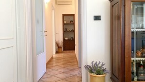 Um corredor com chão de azulejos, um armário de madeira com portas de vidro e uma planta em vaso.