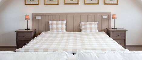 Quarto bem arrumado com colcha xadrez, duas mesas de cabeceira e quadros nas paredes.