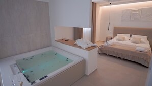 Quarto de hotel moderno com banheira, cama e uma pequena mesa com toalhas.