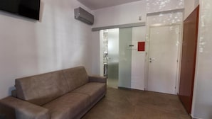 Quarto com sofá, televisão de tela plana, ar condicionado, porta de vidro deslizante e porta de madeira.