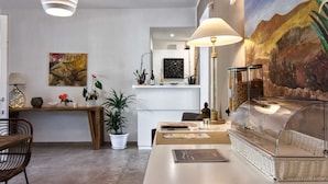 Uma área de recepção com balcão, cadeiras, planta em vaso, quadro e vitrine de vidro.