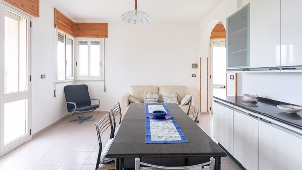 Uma cozinha moderna com armários brancos, uma sala de jantar com mesa e cadeiras, e um sofá.